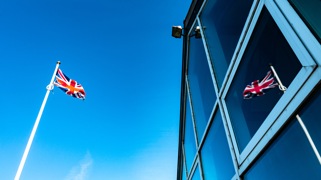 Union Jack flag flying reflecting on office building window - The TRADE
